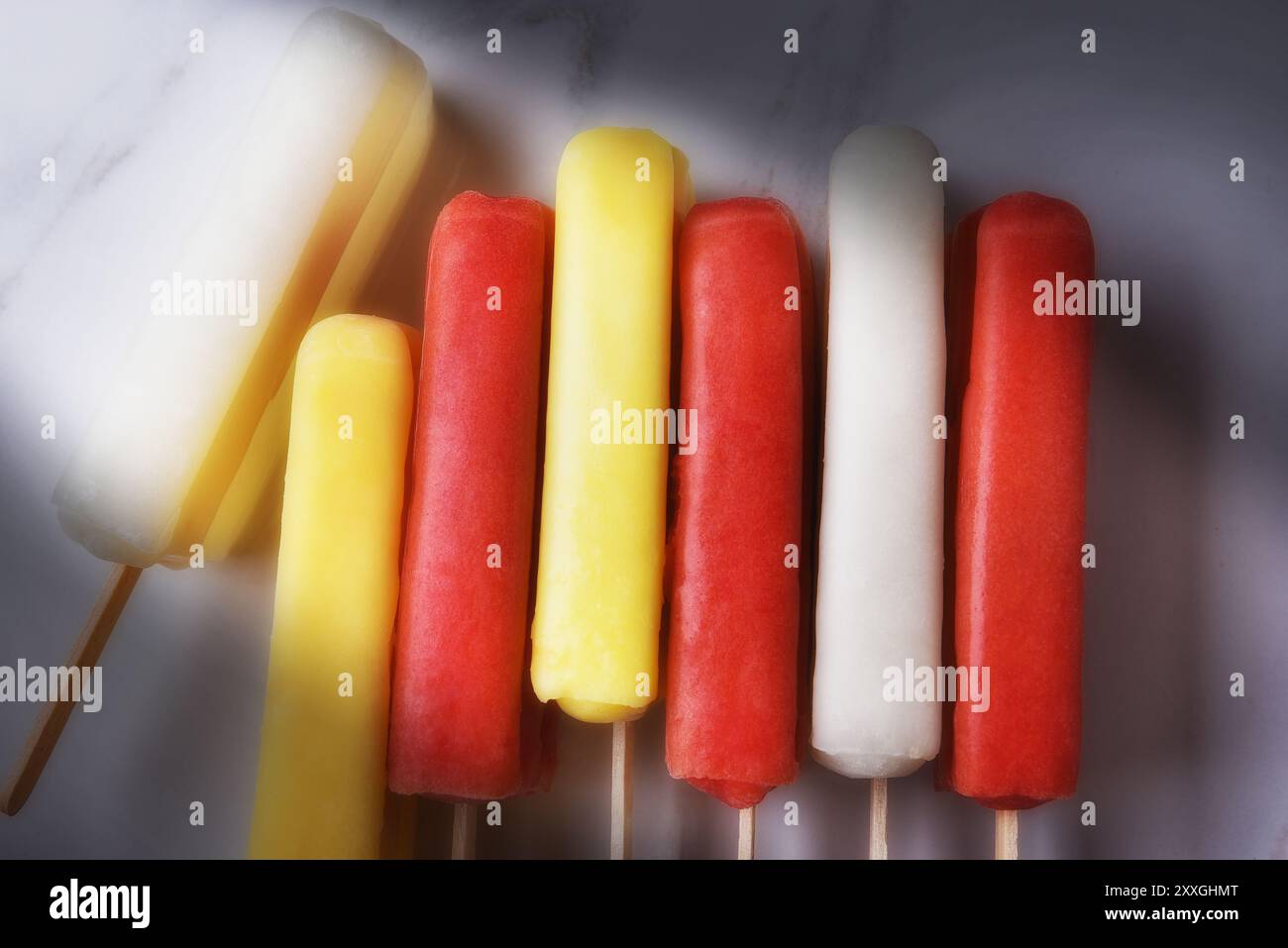 Top view of a group of assorted ice pops on a marble counter top. Red ...