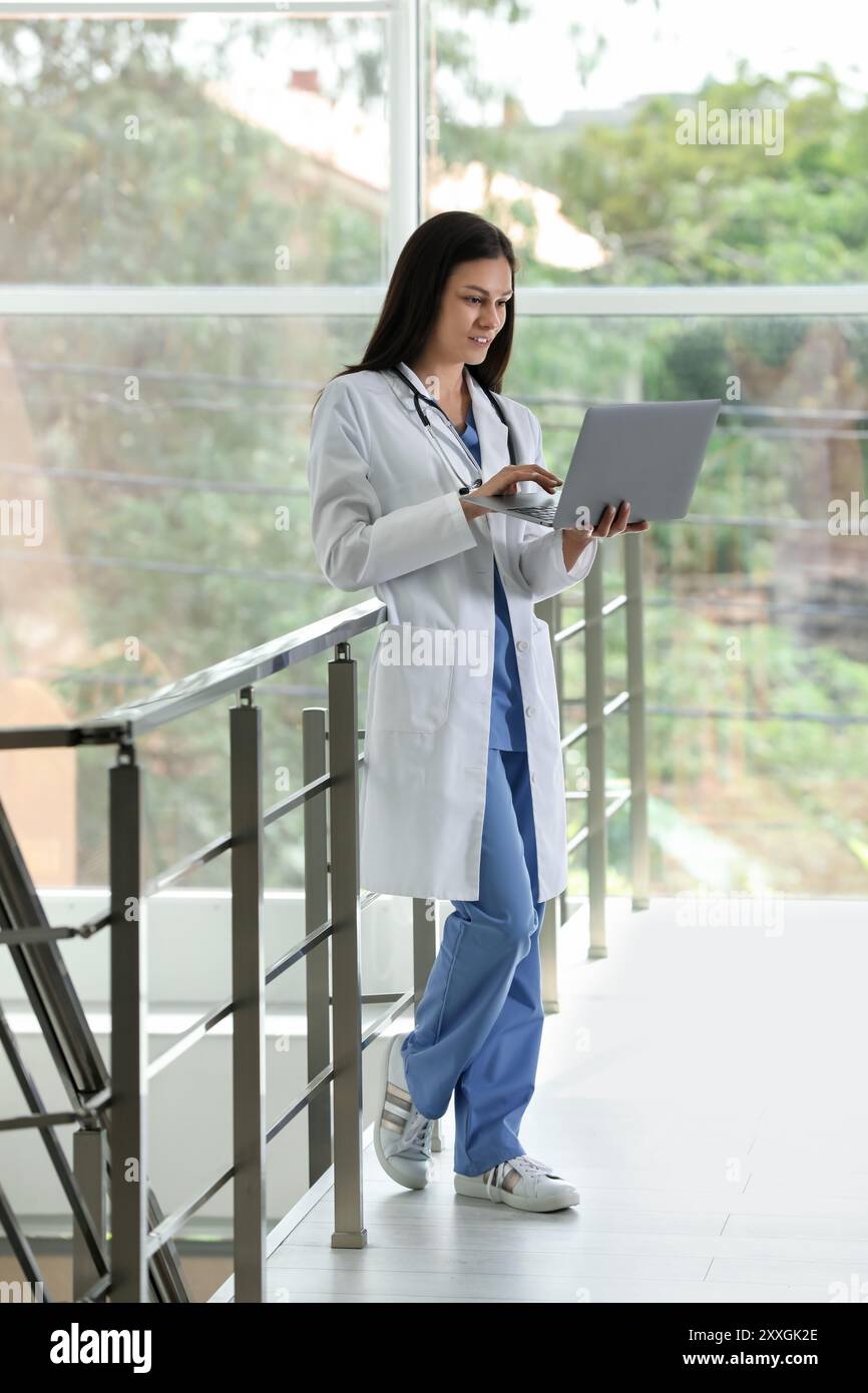 Smiling nurse with laptop near railings in hospital Stock Photo - Alamy