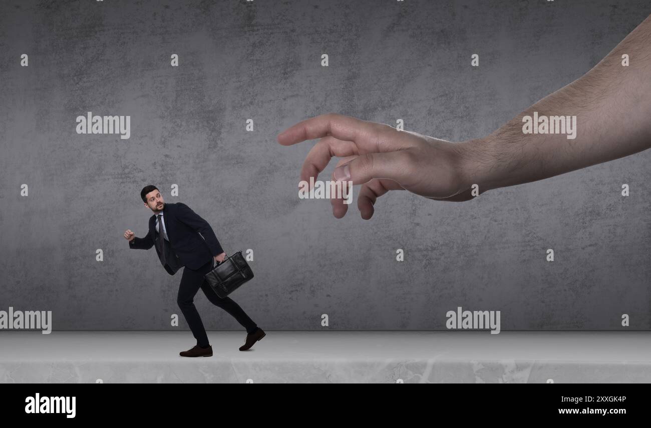 Big hand catching running away small businessman on grey background ...