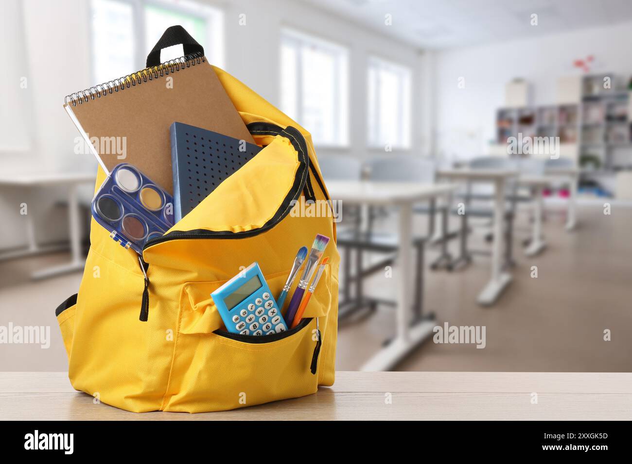 Yellow backpack with stationery on school desk in classroom. Space for ...