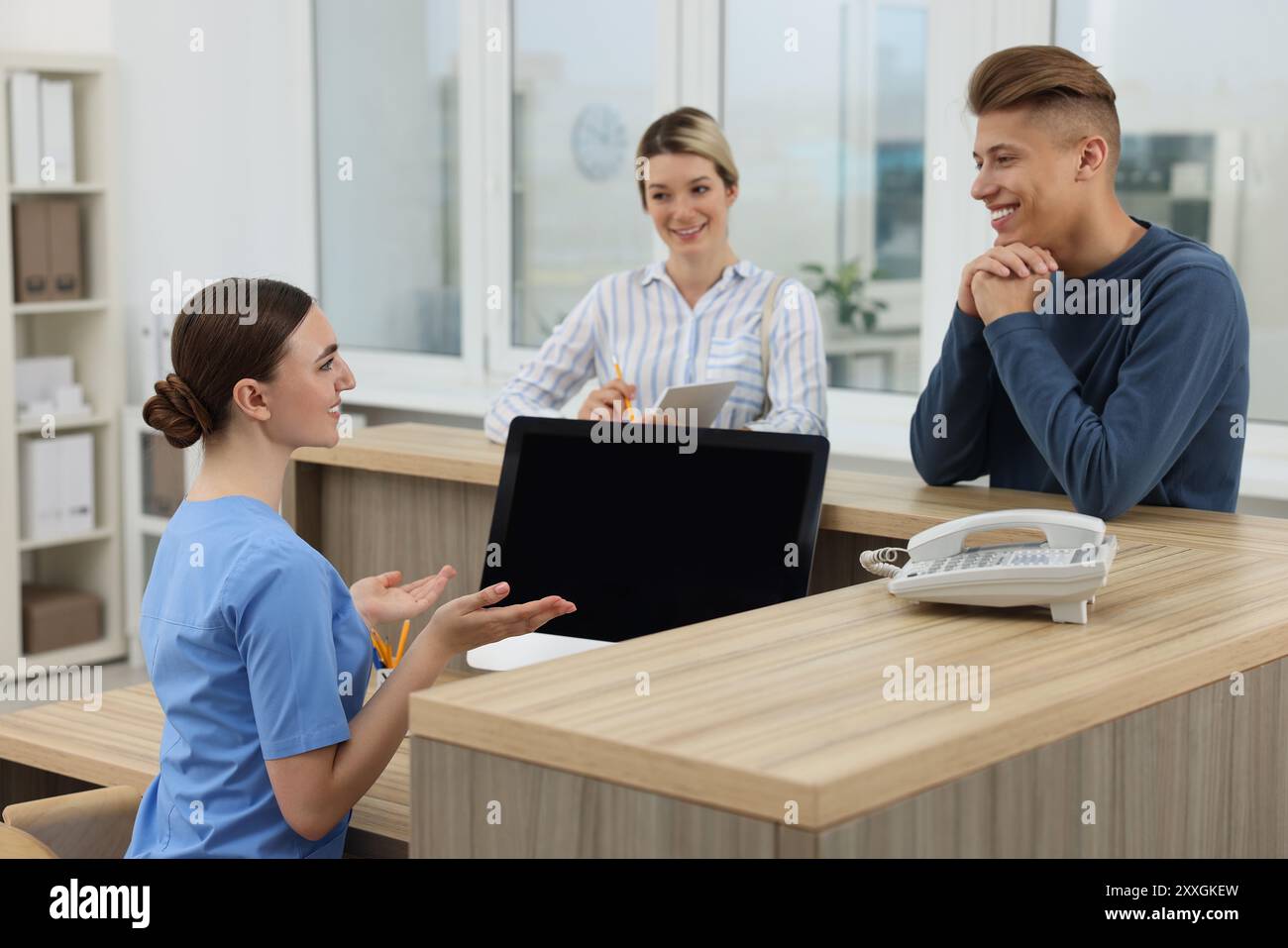Professional receptionist working with patients at wooden desk in ...