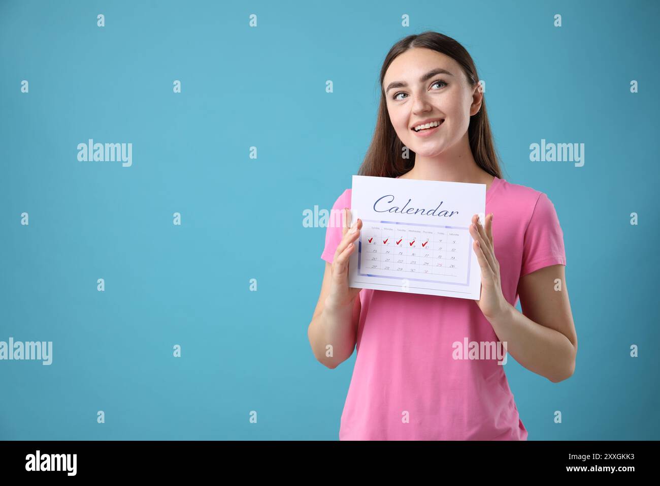 Woman holding calendar with marked menstrual cycle days on light blue ...