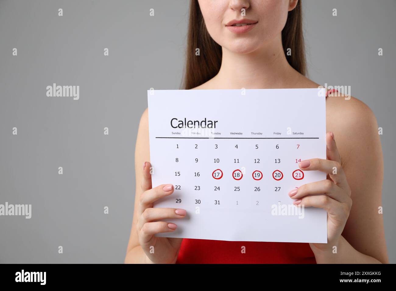 Woman holding calendar with marked menstrual cycle days on grey ...