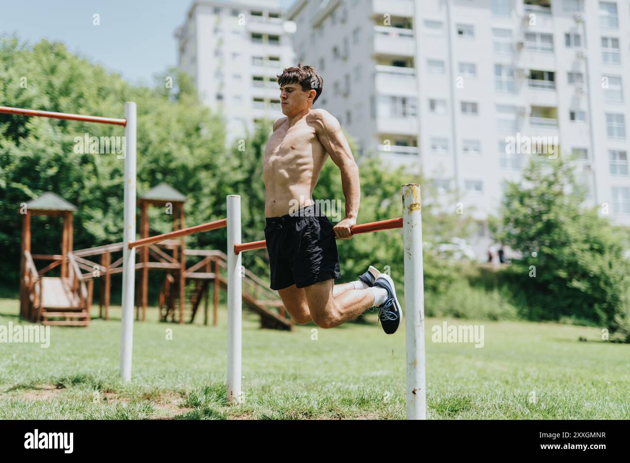 Fit male athlete performing outdoor workout on horizontal bar in urban ...