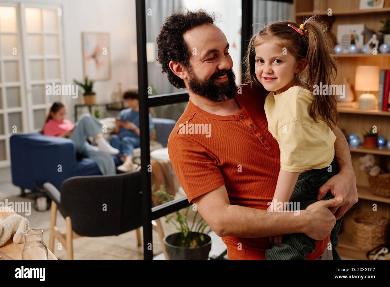 Father smiling while holding his daughter in cozy living room setting ...