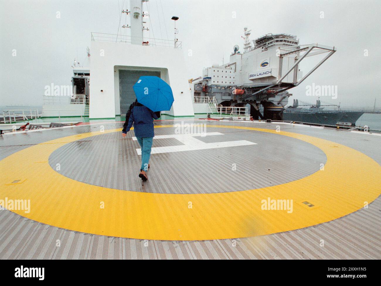 A man with a blue umbrella crossing the helipad on the Kværner Boeing ...
