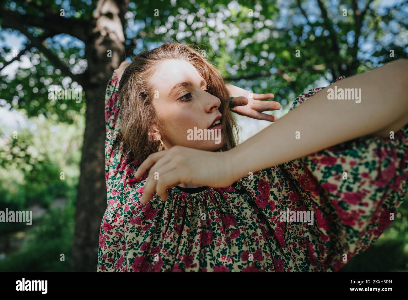 A young girl performing modern dance in a natural setting, wearing a floral dress with sunlight ...