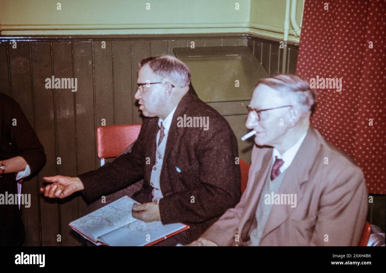 Two men sitting talking with friends at a social event in the 1960s ...