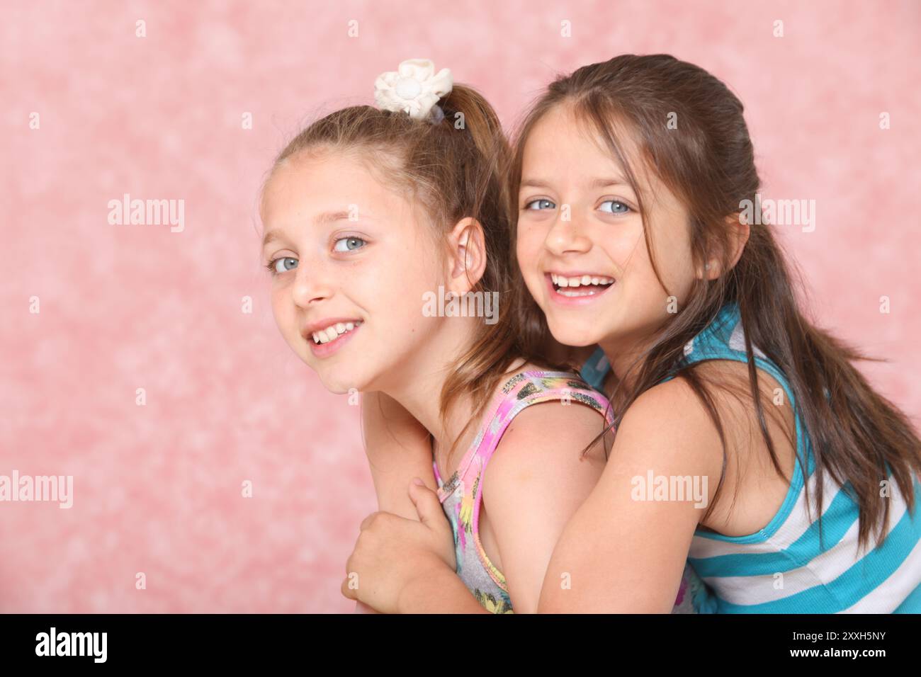 portrait of two cheerful preteen girls laughing on pink background ...