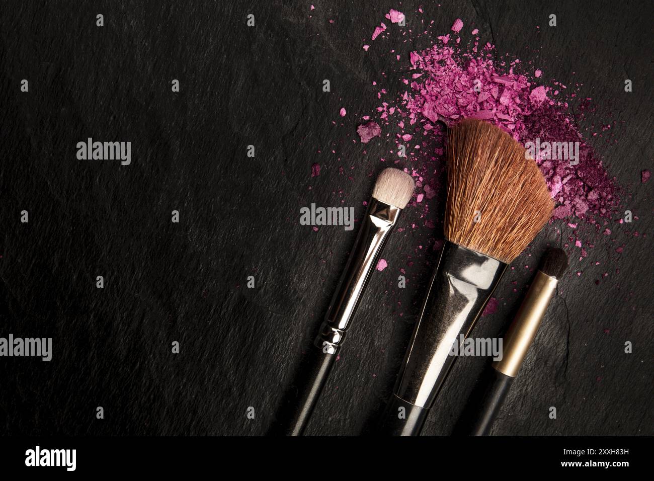 Make-up brushes with crushed cosmetics, shot from the top on a black ...