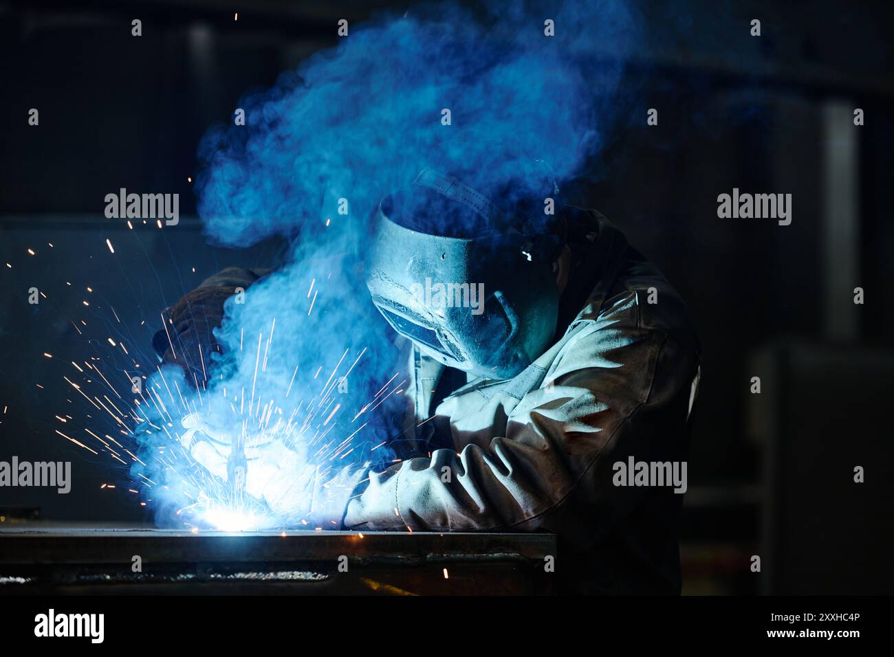 Metal worker performing welding with sparks flying in workshop, wearing ...