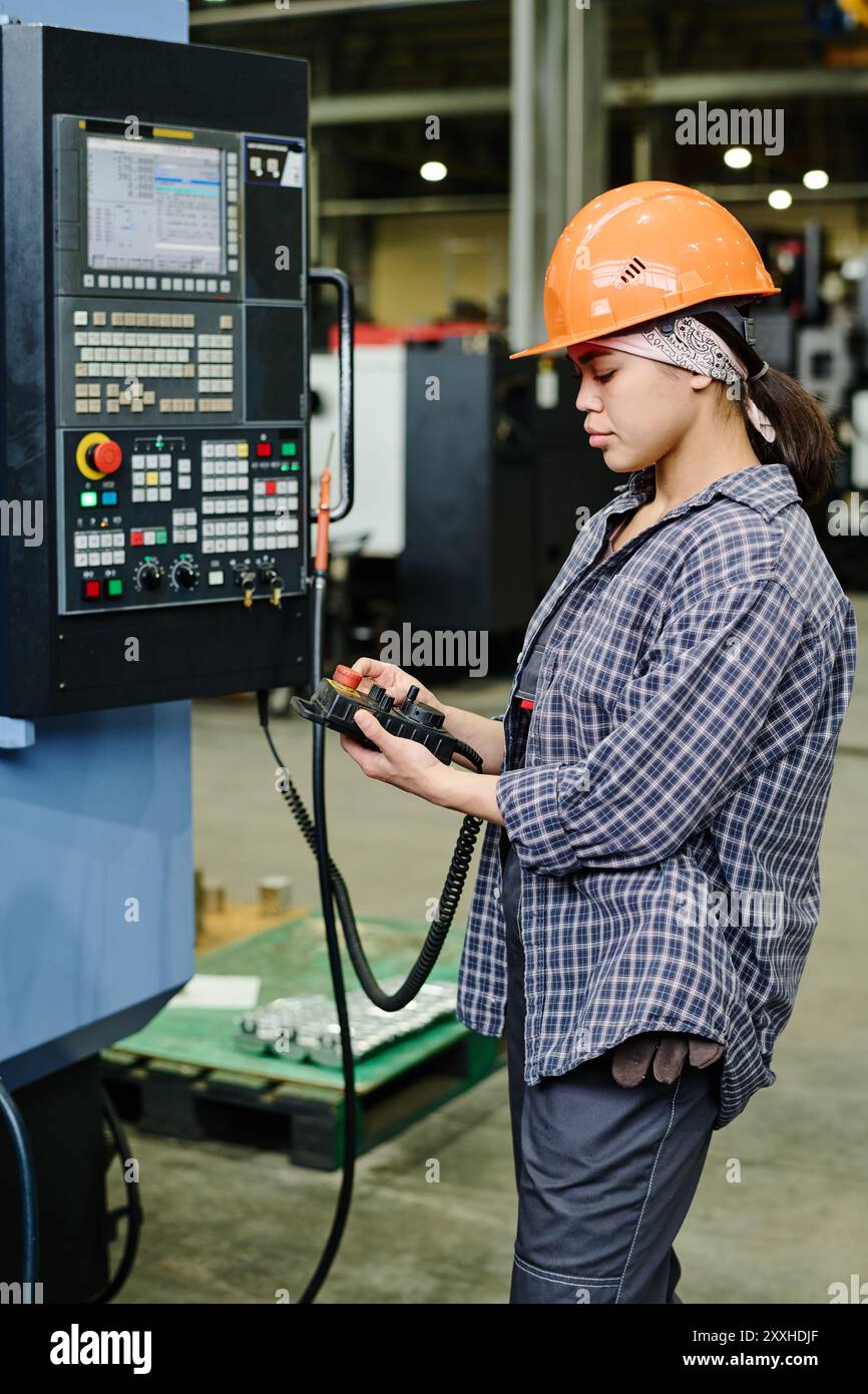 Worker in factory operating industrial machine using control panel ...