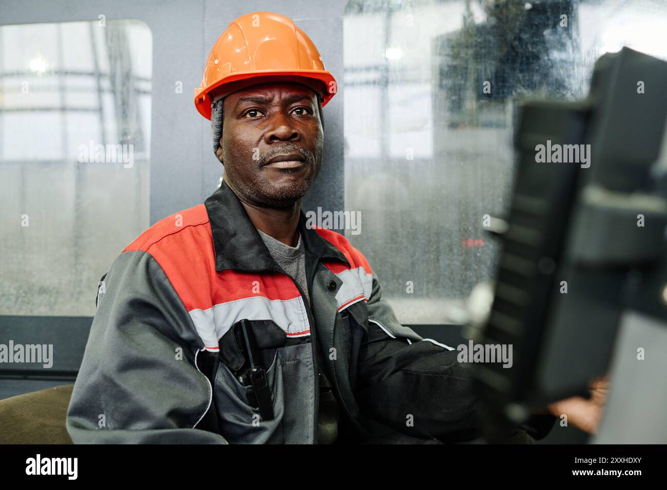 Portrait of man wearing orange hard hat and work uniform seated indoors ...
