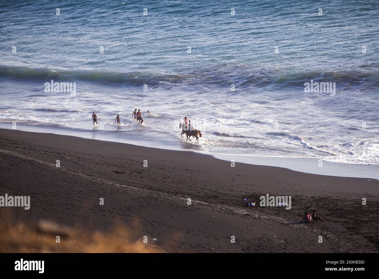 Two riders on horses ride along a beach, past people bathing Stock ...