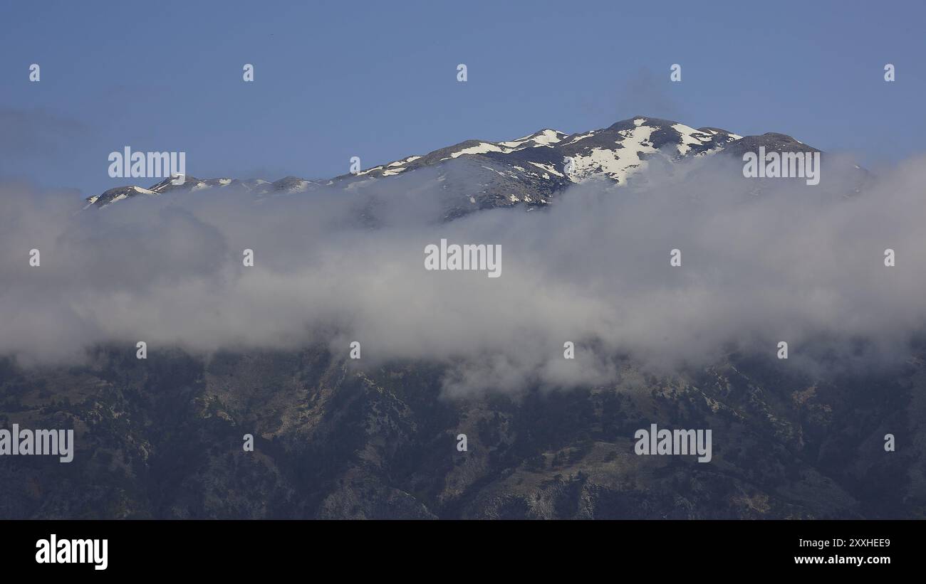 Mountain peak partially obscured by clouds and fog, with a snow-capped ...