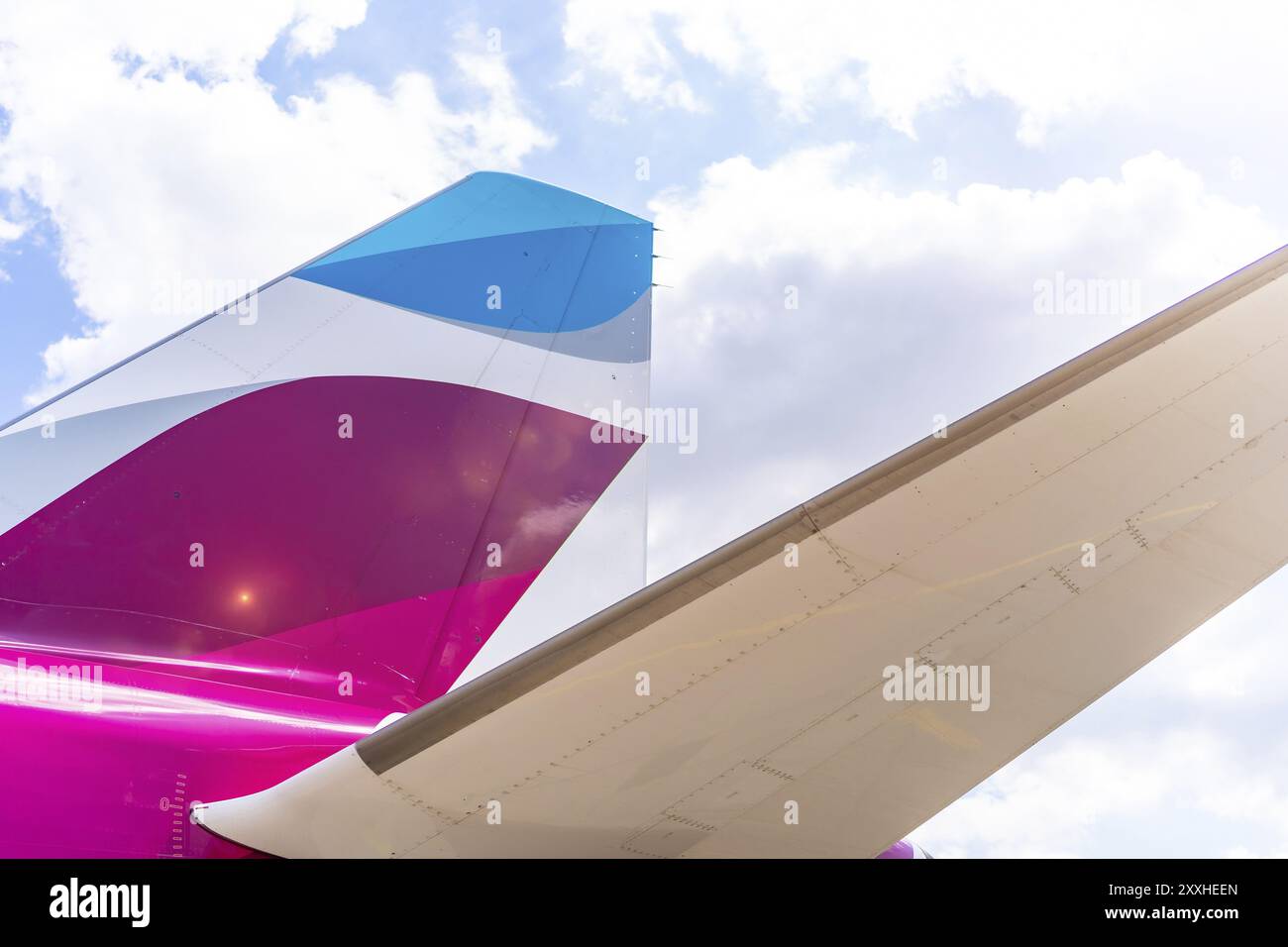 The tail of a plane is shown in a close up. The tail is pink and blue ...