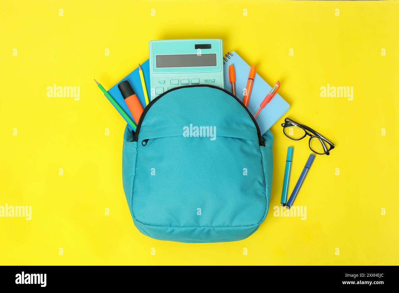 Light blue backpack and different school supplies on yellow background ...
