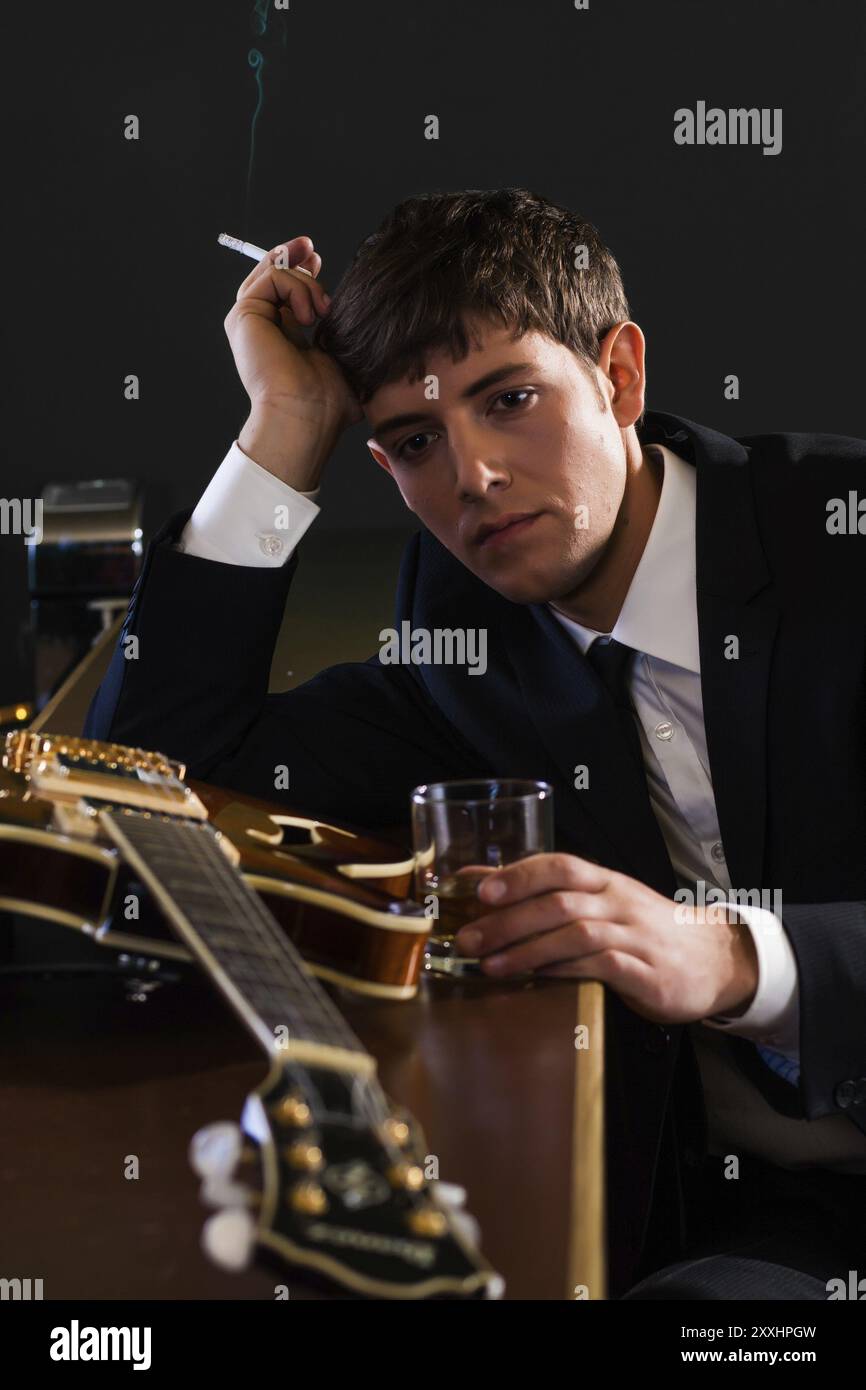 Young man in a suit sitting at a bar with his guitar, drinking alcohol ...