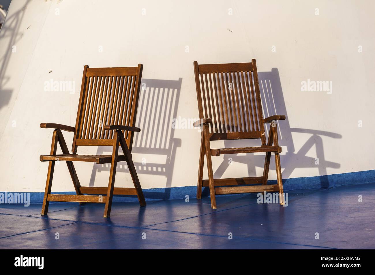 Two brown deck chairs are standing on a sun deck in the bright sunlight ...