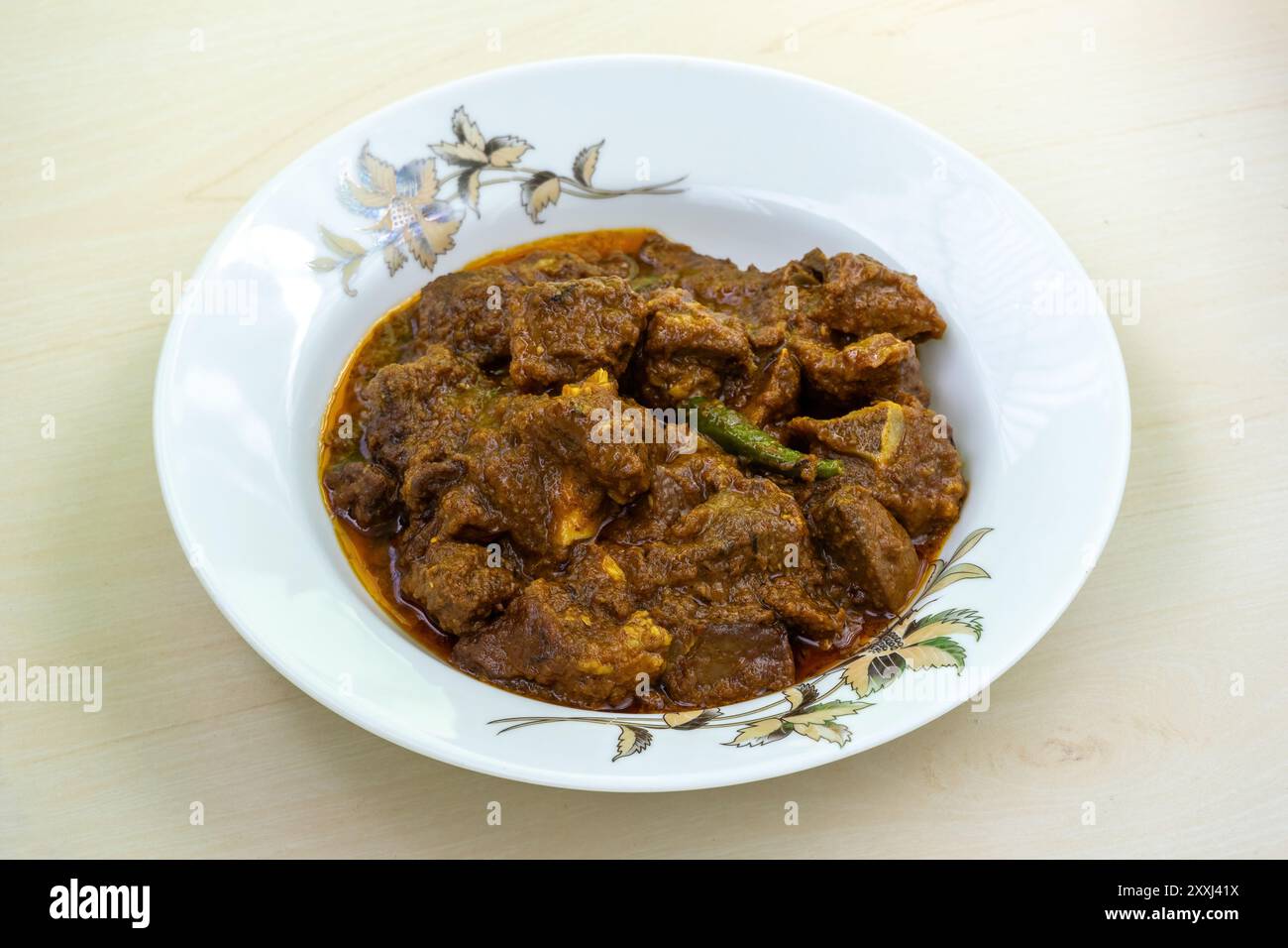 Delicious mutton curry in a white ceramic plate on a wooden background ...