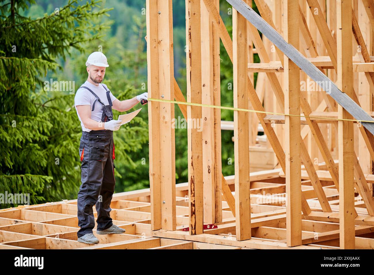Carpenter building wooden skeleton house. Man measures distances with ...