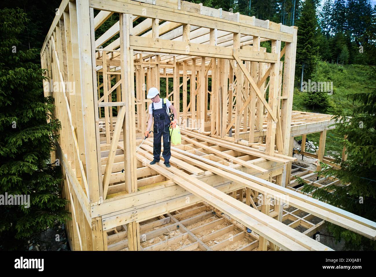 Laborer constructing wooden frame house near forest. Man treating woods ...