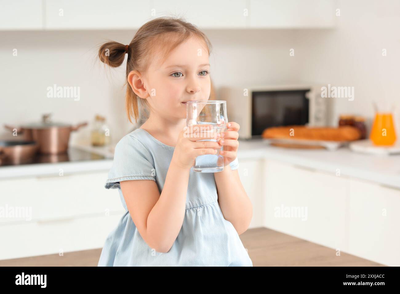 Cute little girl drinking water in kitchen Stock Photo - Alamy