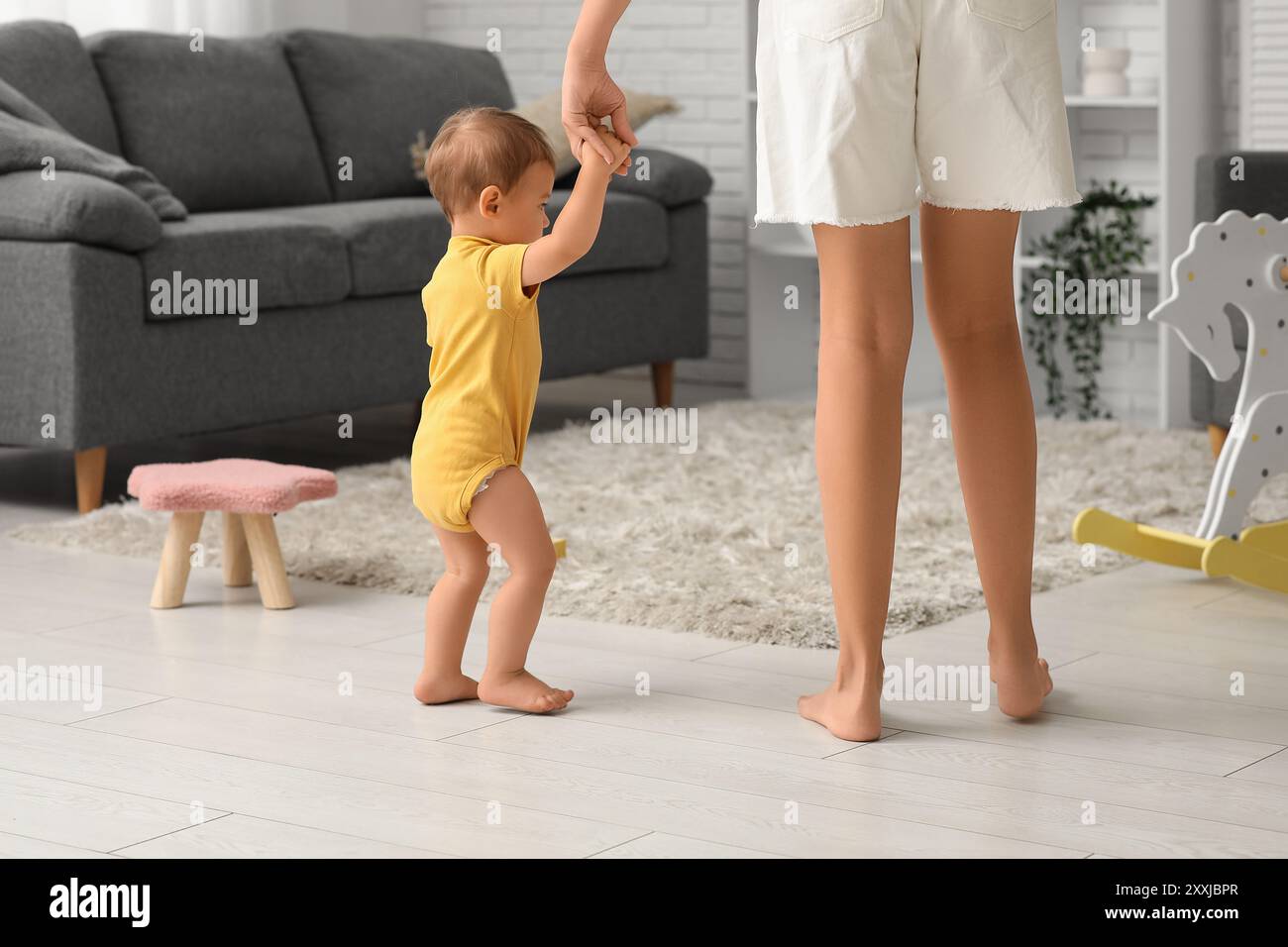 Cute little baby girl learning to walk with mother at home, back view ...