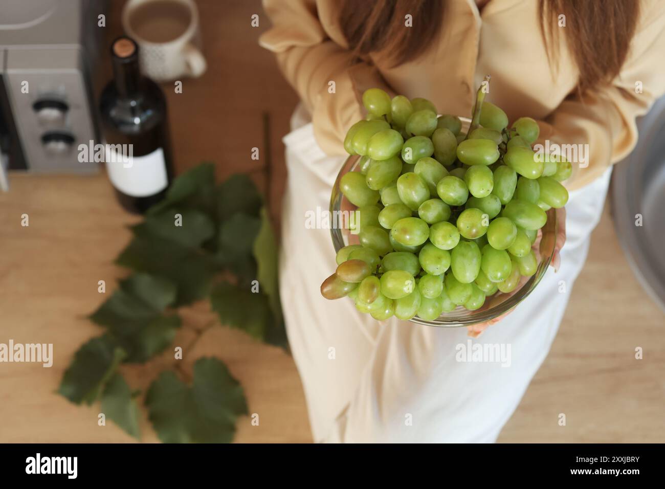Young woman with green grapes sitting on counter in kitchen, closeup ...