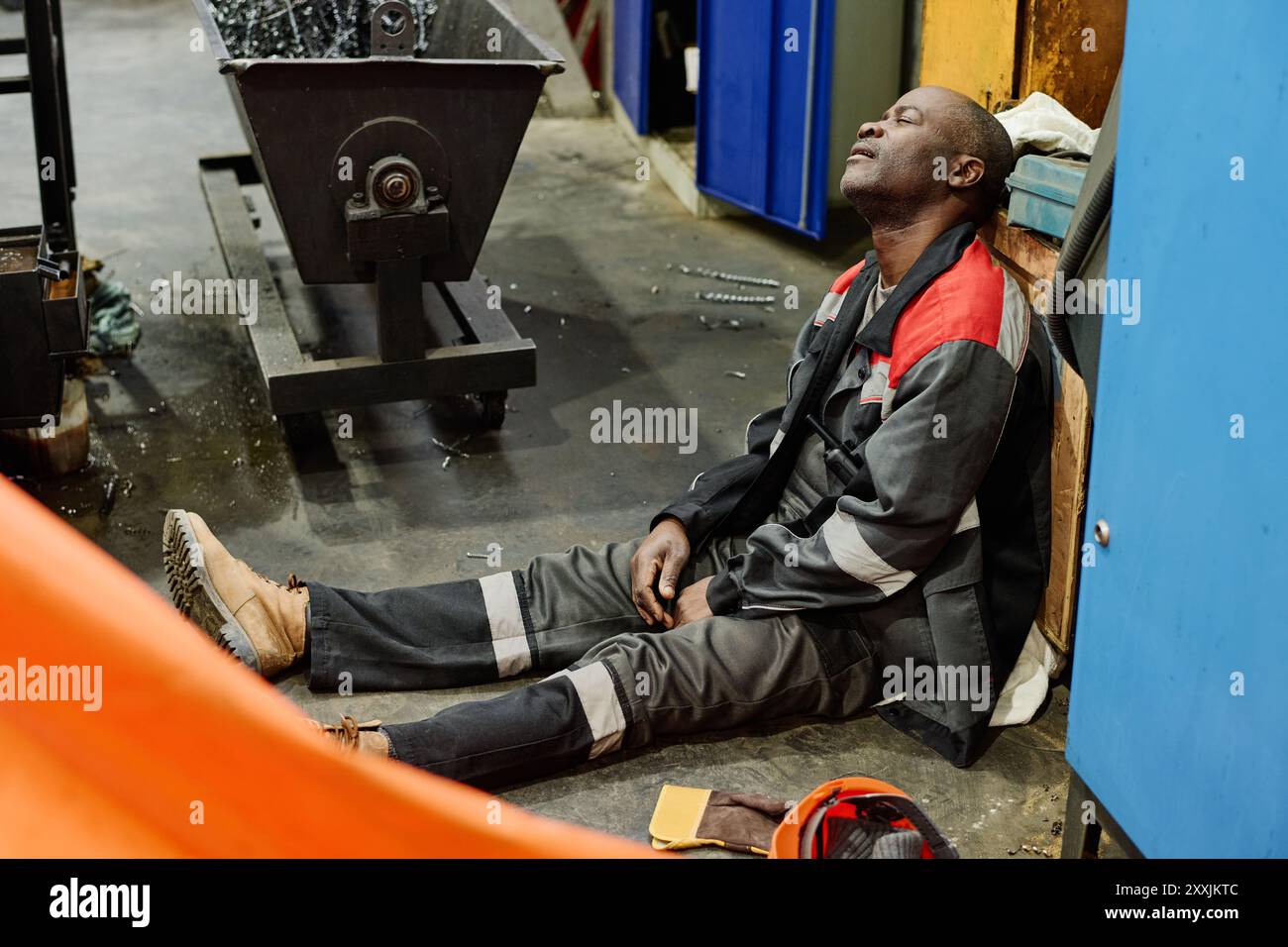 Worker sitting against wall in industrial setting, appearing exhausted ...