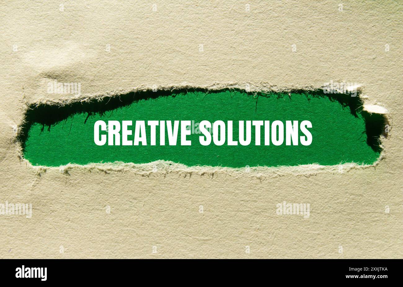 Creative solutions message written on ripped torn paper with green background. Conceptual ...