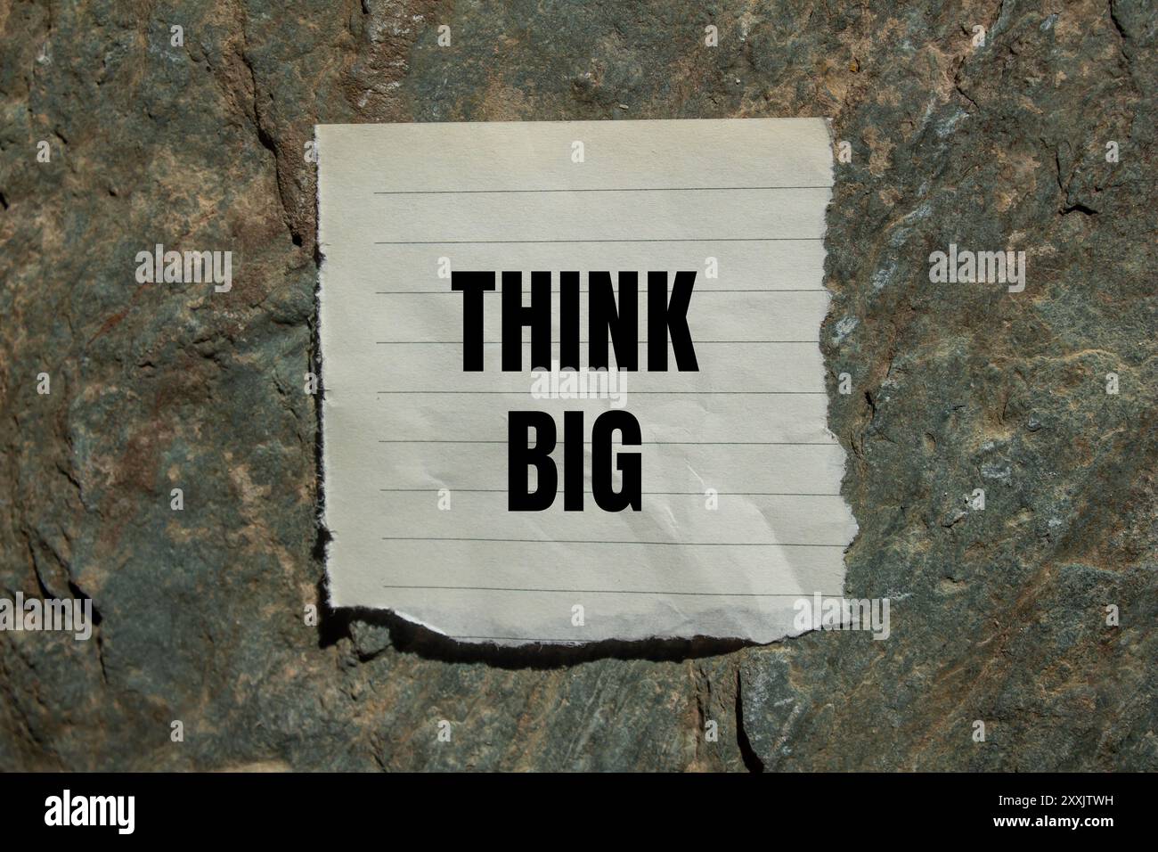 Think big message written on ripped torn paper piece with stone background. Conceptual think big ...