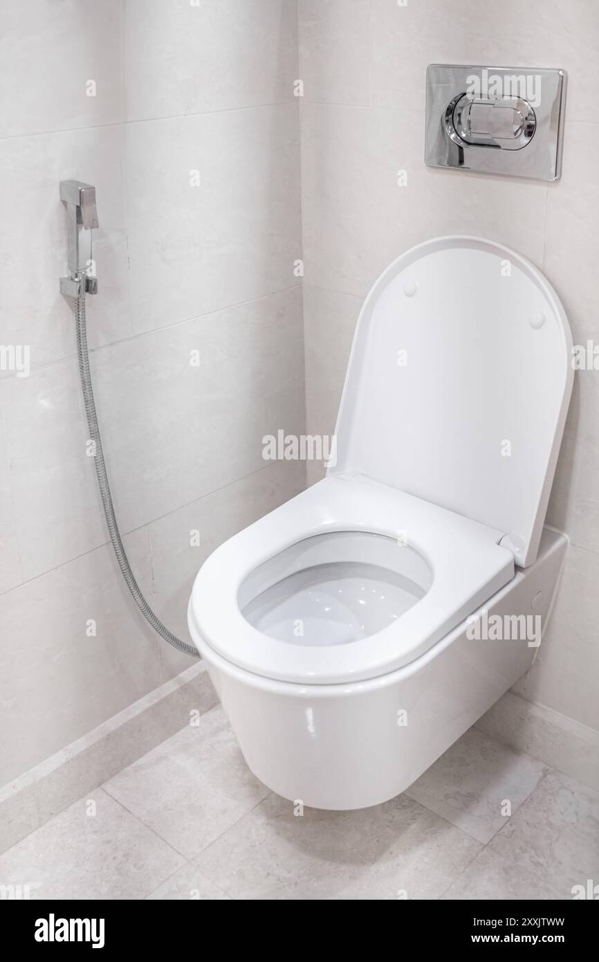 White toilet seat with a hose for flushing water hanging on the wall ...