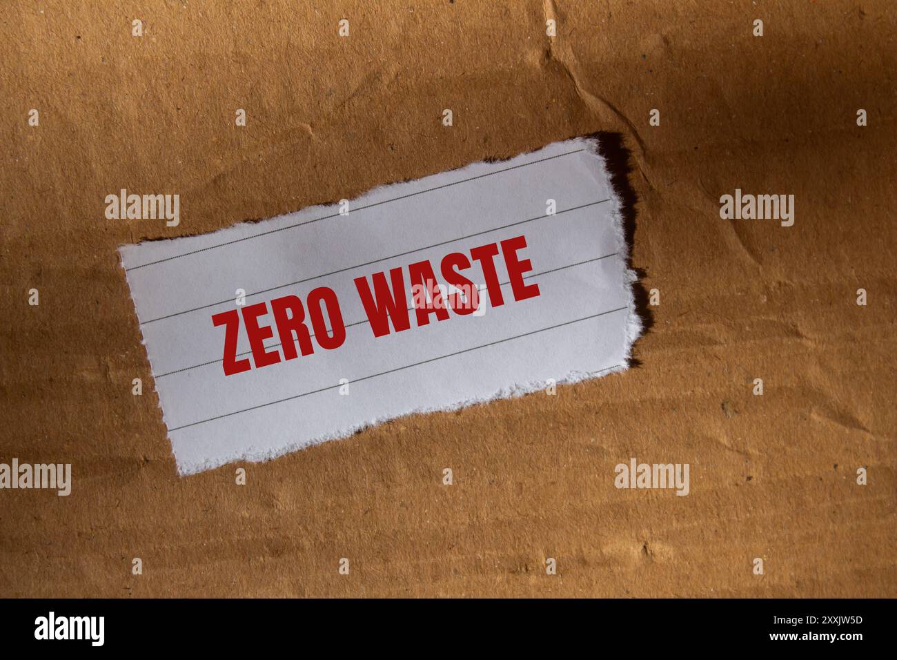 Zero waste message written on ripped torn white paper piece with cardboard background ...