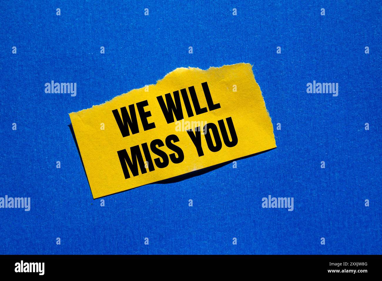 We will miss you message written on ripped torn yellow paper piece with bluebackground ...