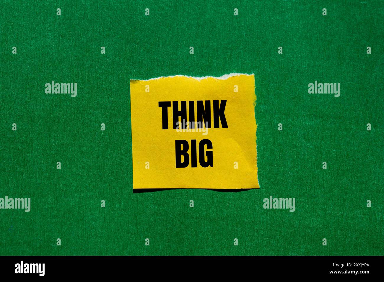 Think big message written on ripped torn yellow paper piece with green ...