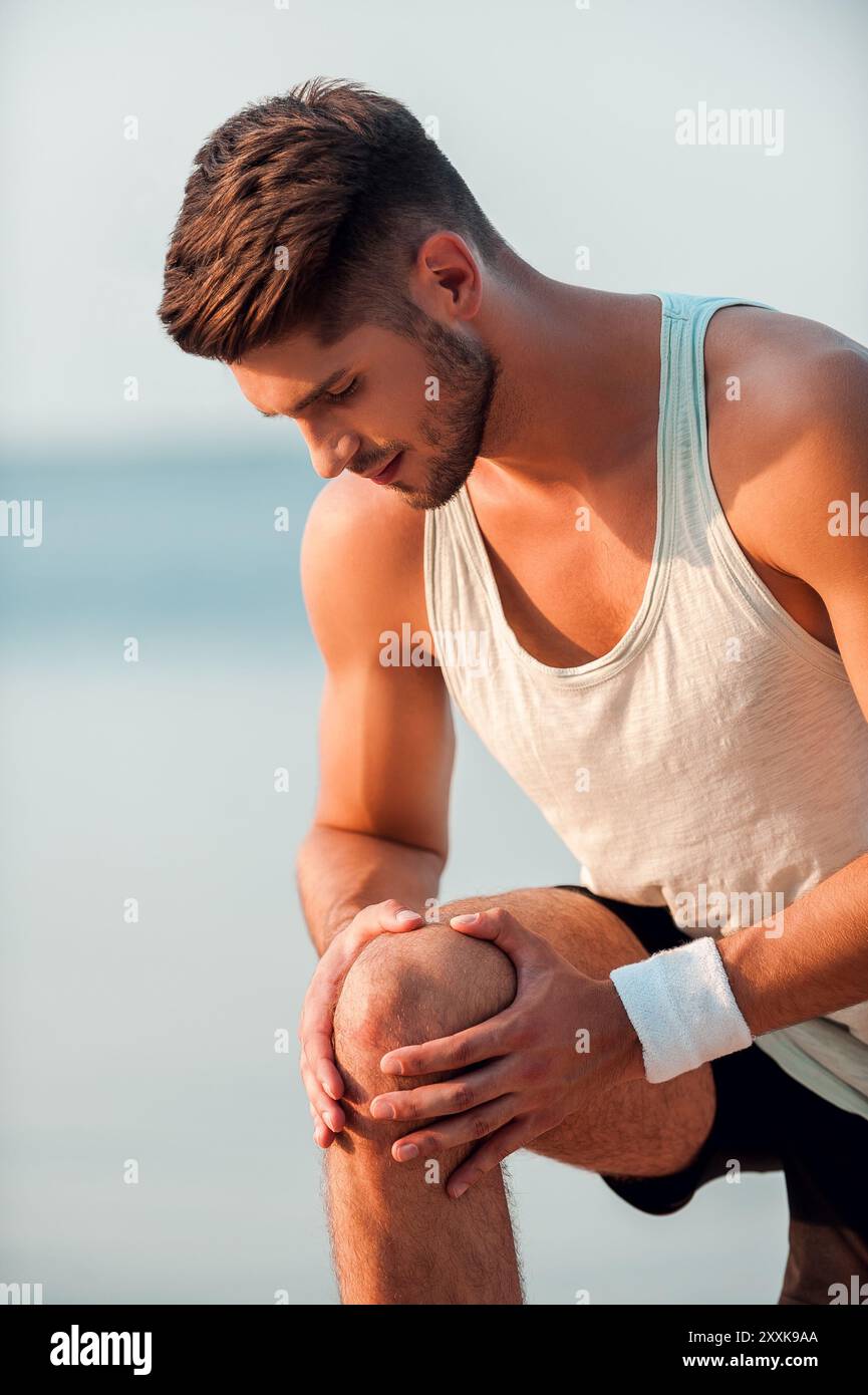 Feeling pain in his knee. Concentrated young muscular man massaging ...