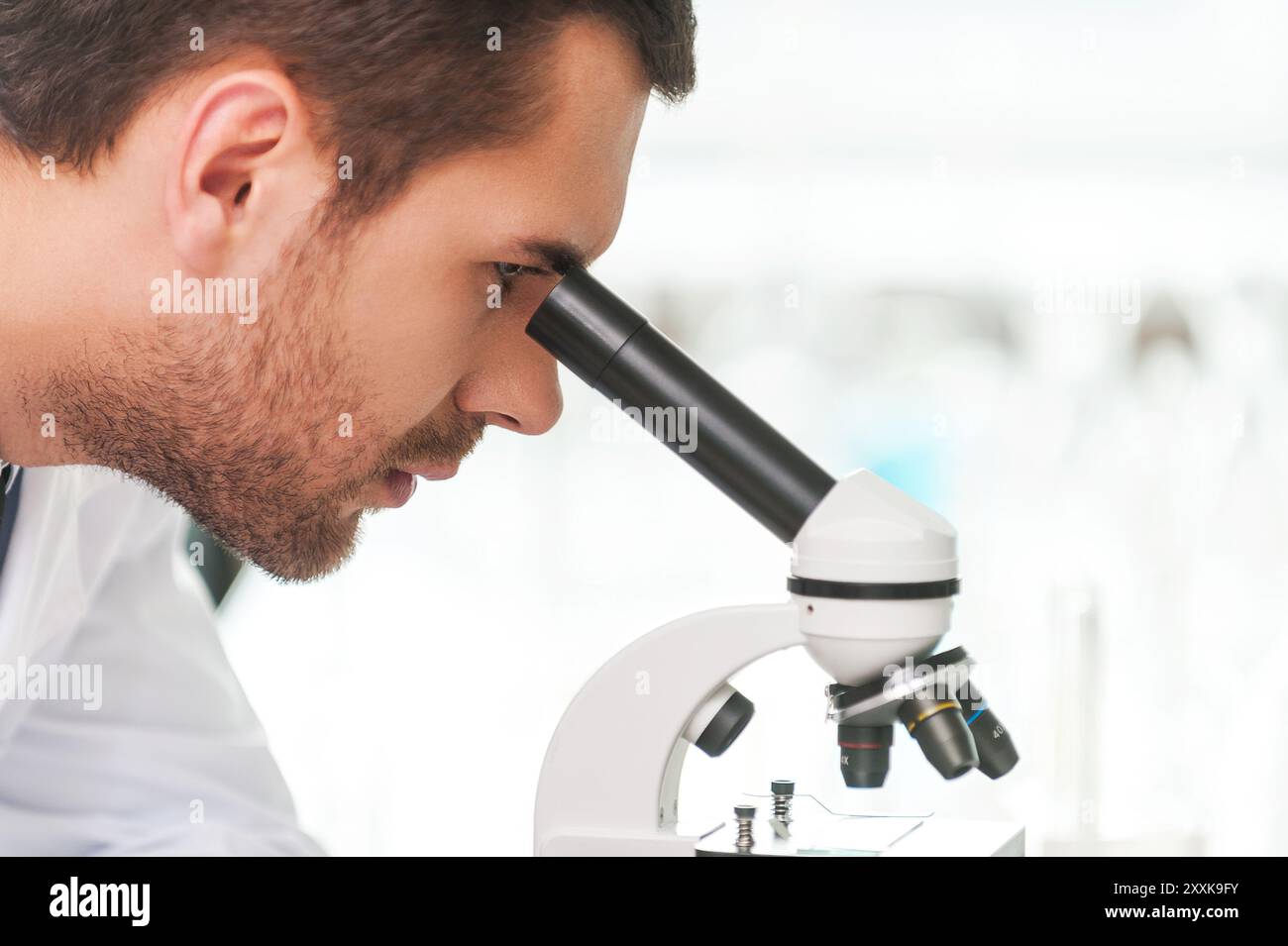 Concentrated on cure. Side view of young scientist in white uniform ...