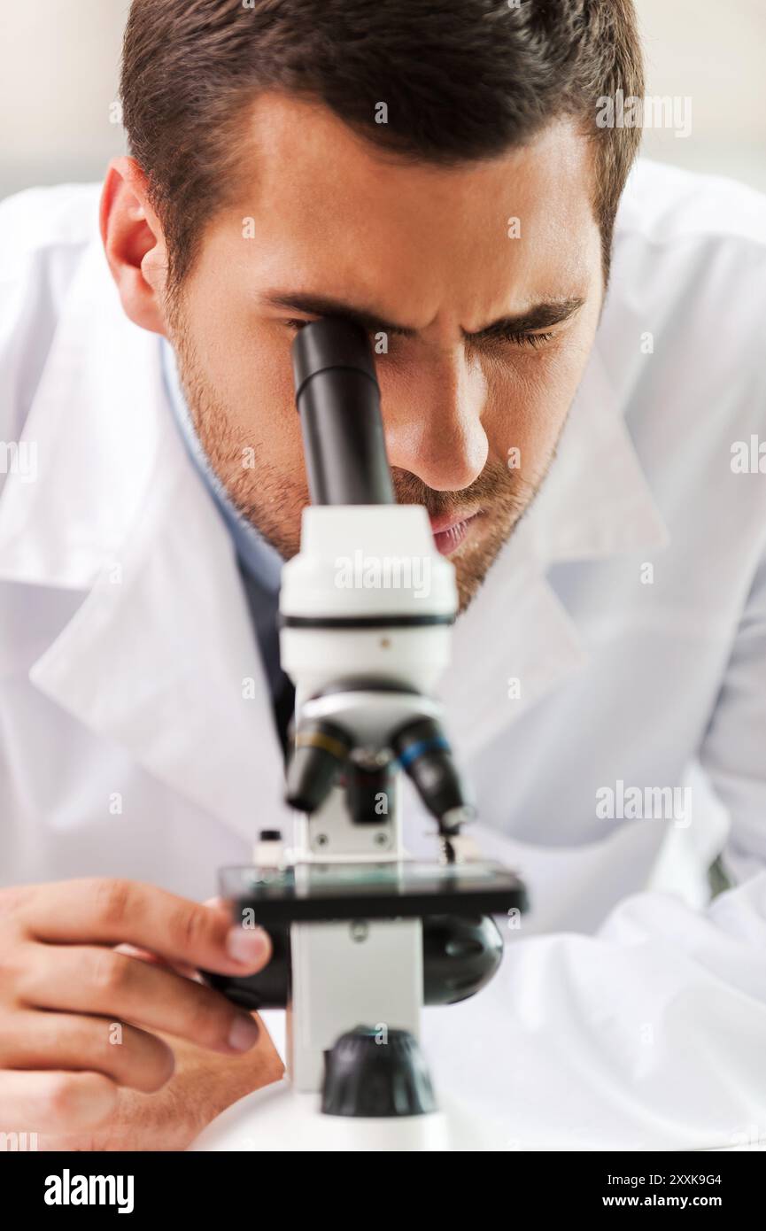 Life under microscope. Concentrated young scientist in white uniform ...