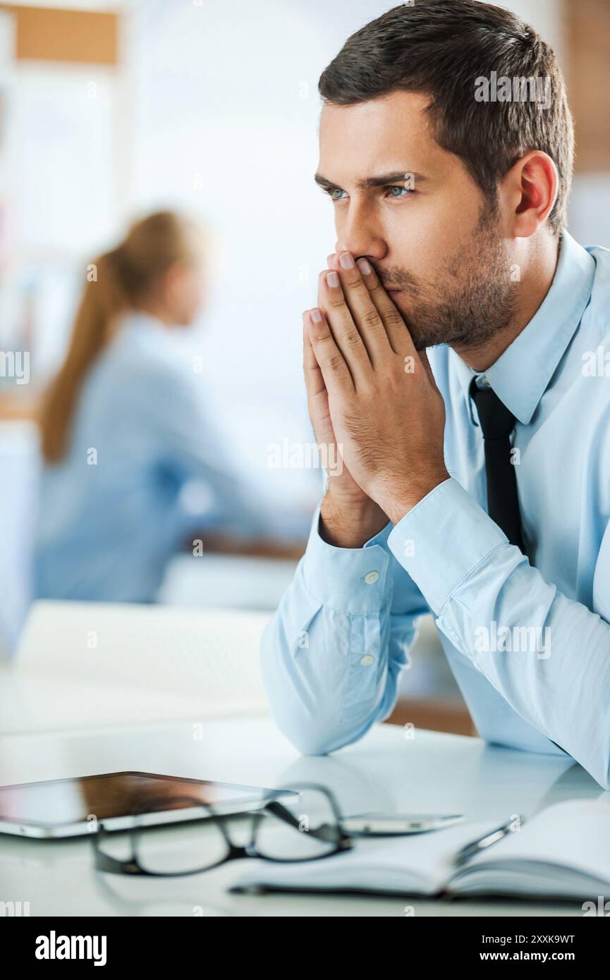Thinking about solution. Serious young businessman in formalwear keeping hands clasped while ...