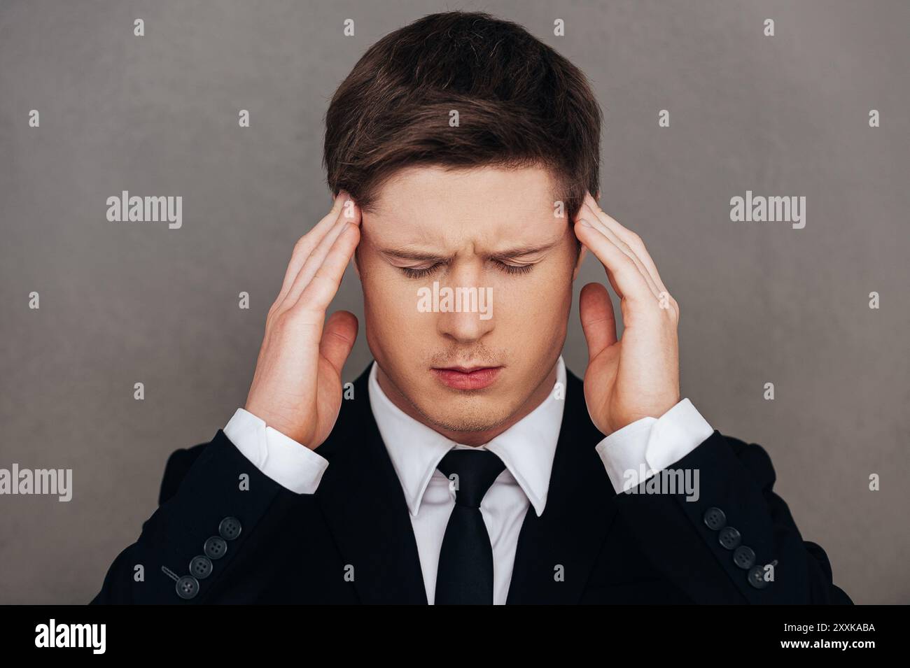 Too much stress. Frustrated young man in formalwear touching head with hands and keeping eyes ...