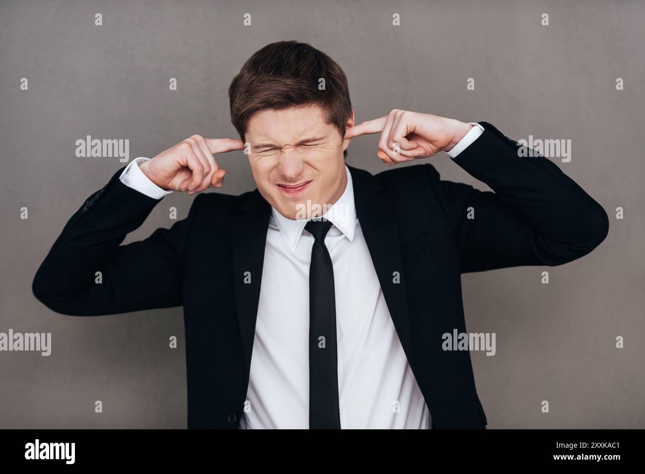 This sound is too loud. Frustrated young man in formalwear closing his ...