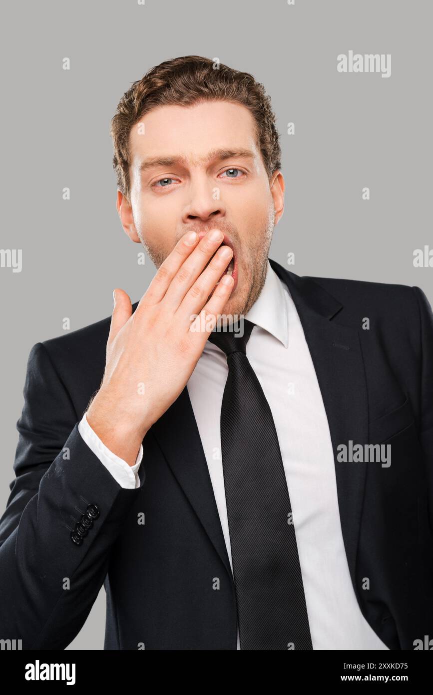 Feeling bored. Bored young man in formalwear covering his mouth by his ...