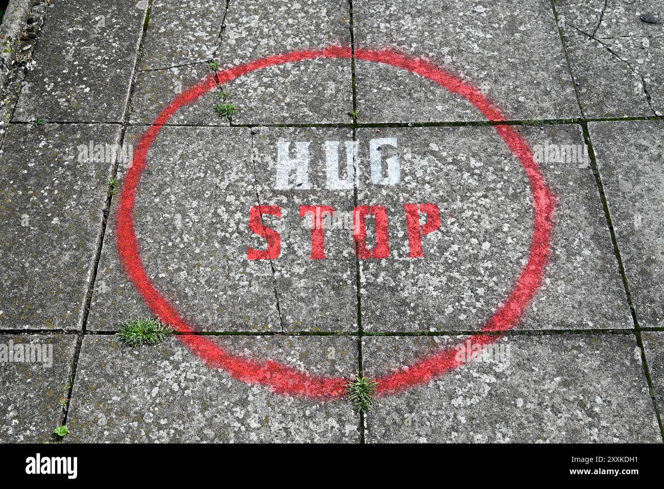 Red and white sign painted on a pavement stating hug stop. August 2024 ...
