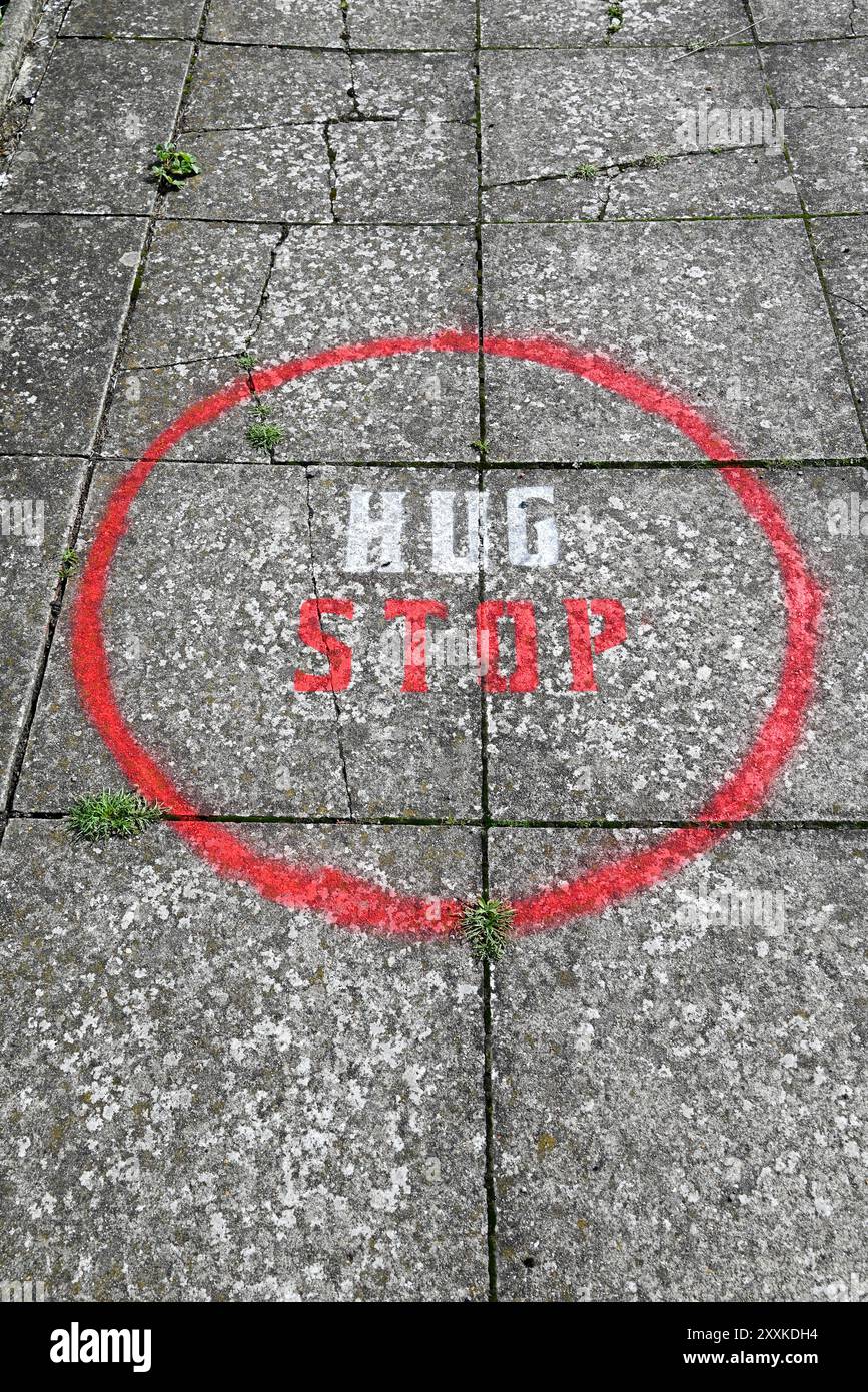 Red and white sign painted on a pavement stating hug stop. August 2024 ...