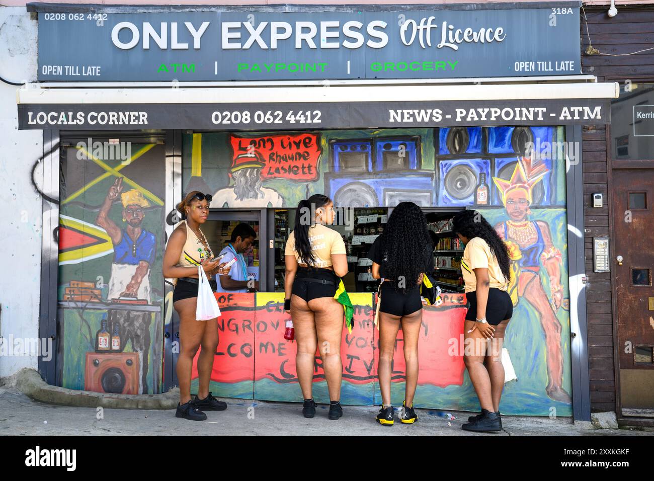 Carnival goers in front of a mural designed by artist, Kudi, on the Only Express corners shop in ...