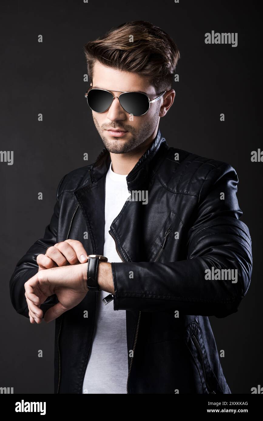 I will be in time. Handsome young man in sunglasses watching time while ...