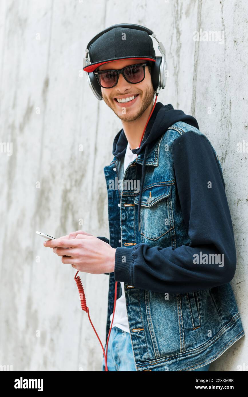 Music lover. Happy young man in headphones holding mobile phone while ...