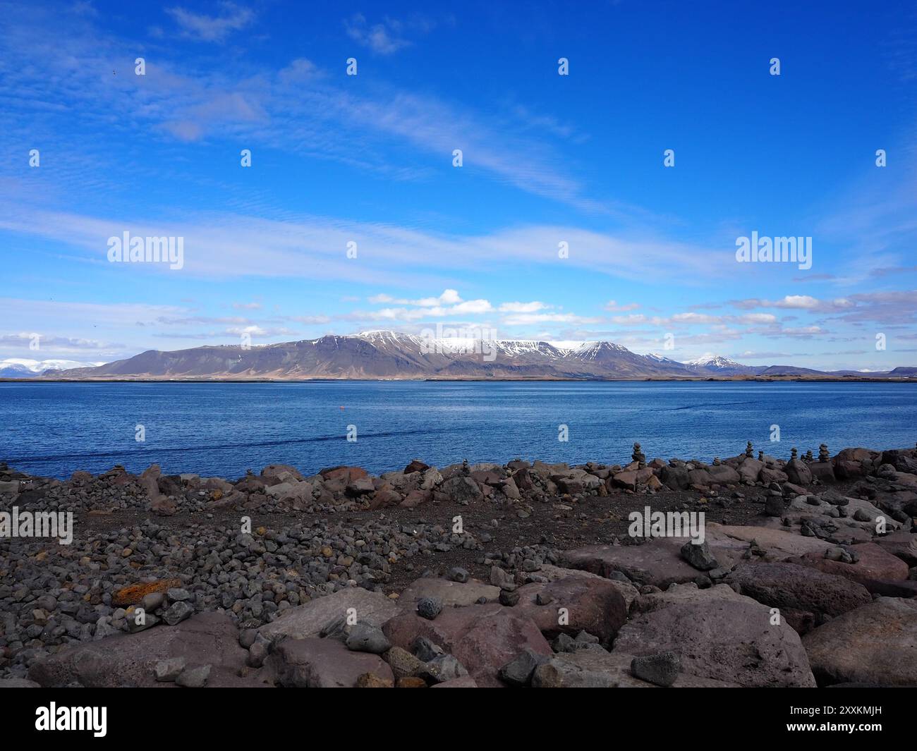 A rocky shoreline stretching parallel to calm blue waters, with snow ...