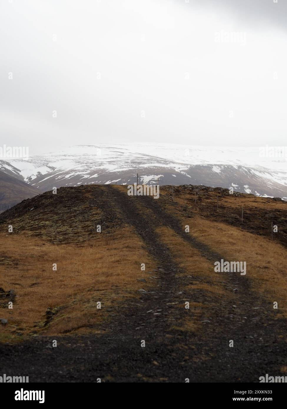 A secluded gravel road winds along a ridge, flanked by snowy mountain ...